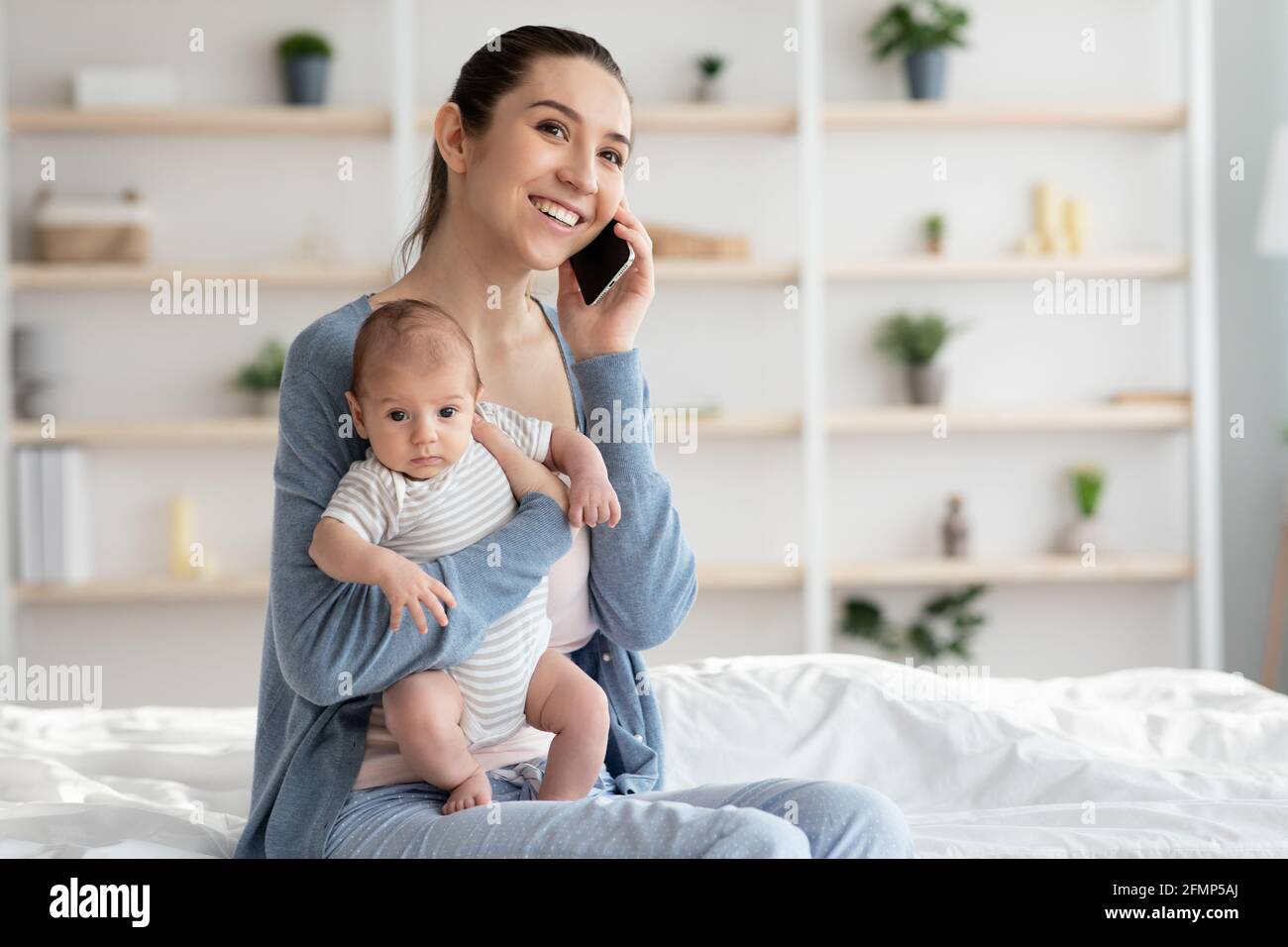 Young mother's lifestyle concept. Smiling mom talking on phone, holding ...