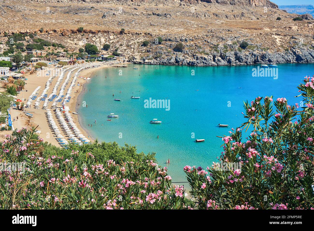 Sunbed rows on sandy Lindos beach near turquoise sea with motorboats ...
