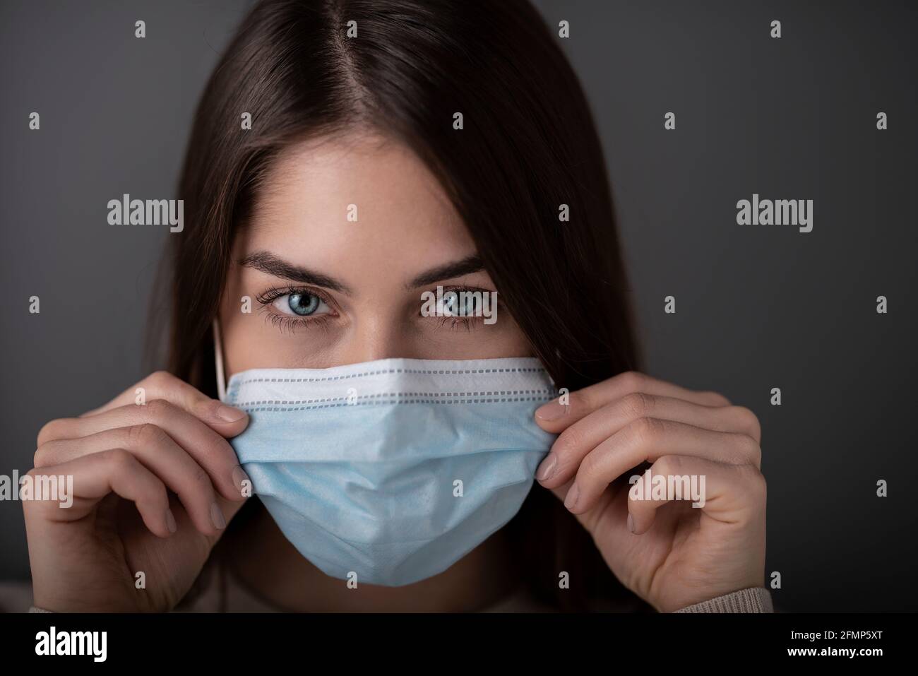 Studio portrait of young woman puting on a face mask while standing at ...