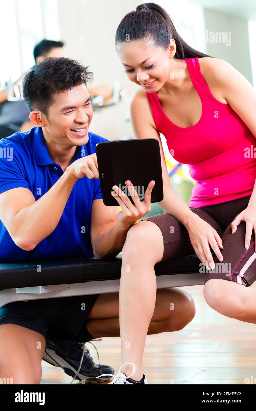 Asian Chinese Woman and personal fitness trainer in gym discussing ...