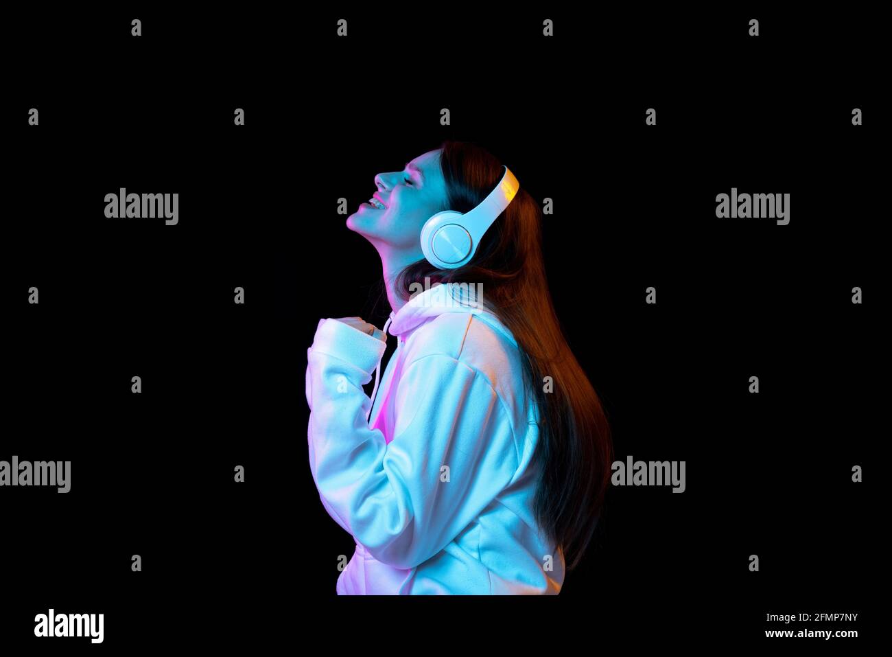 Side view of young beautiful girl isolated over dark background in neon ...