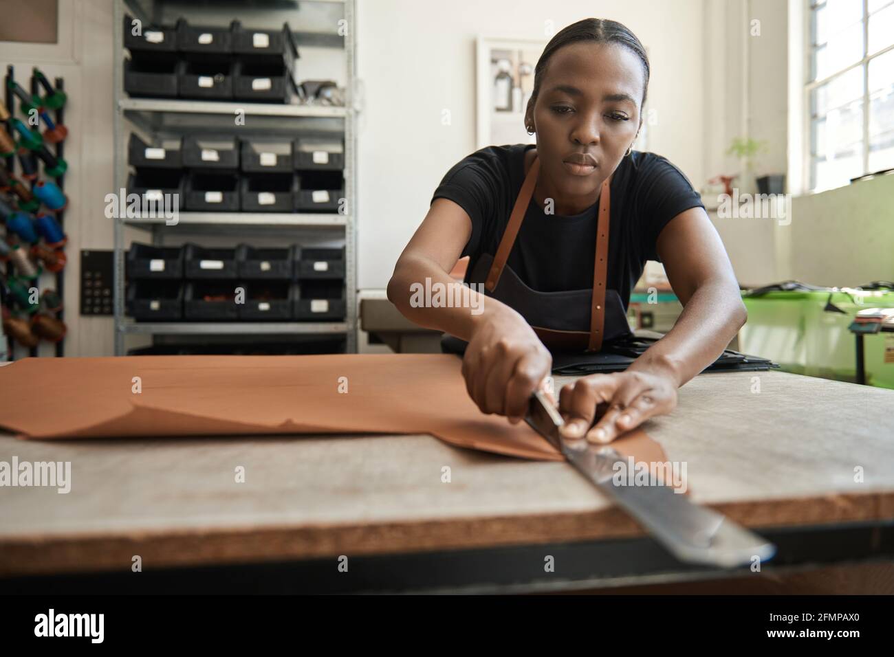 Young African female artisan cutting leather at a workbench Stock Photo ...