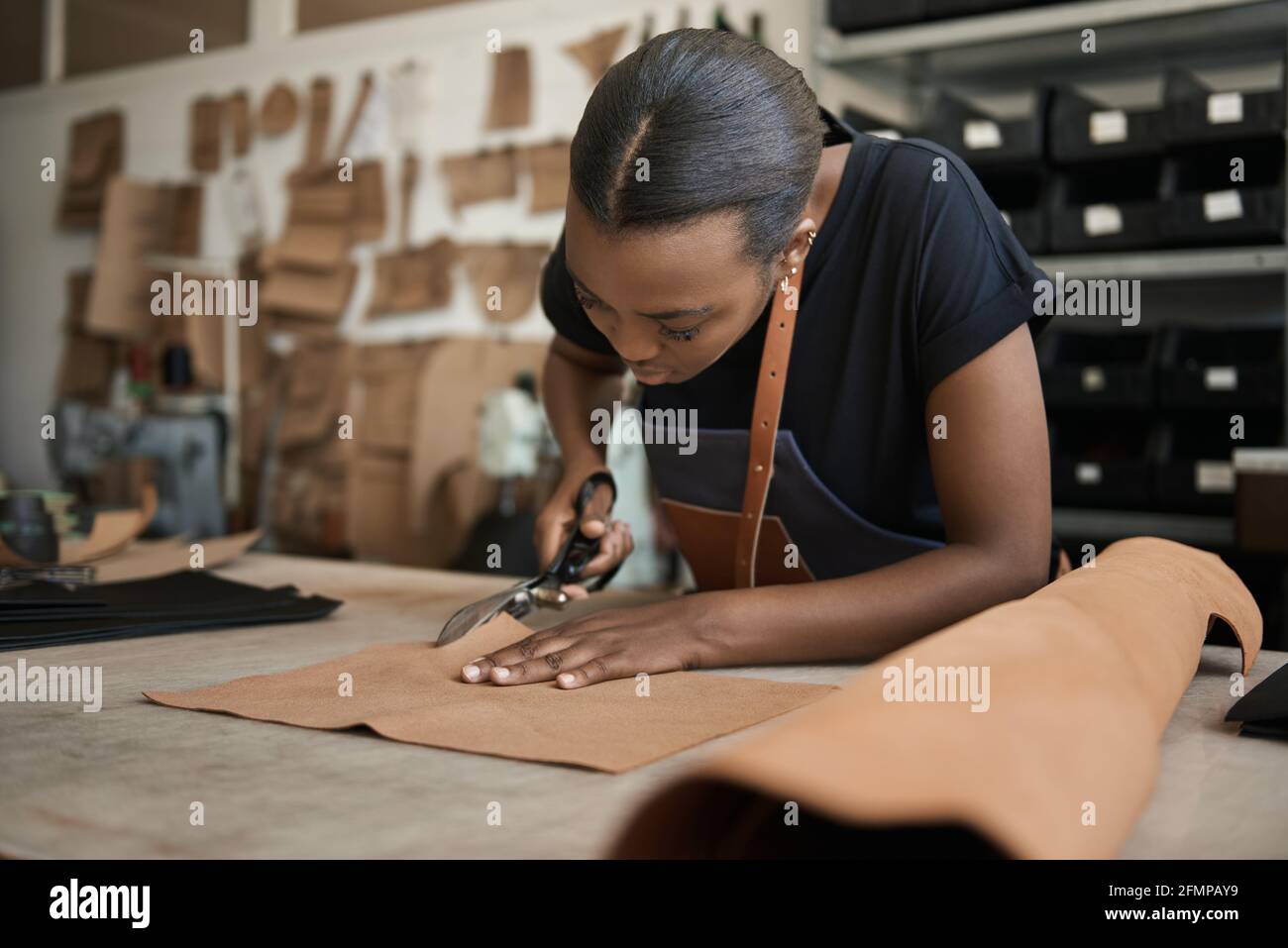 Young African female artisan cutting leather in her workshop Stock ...