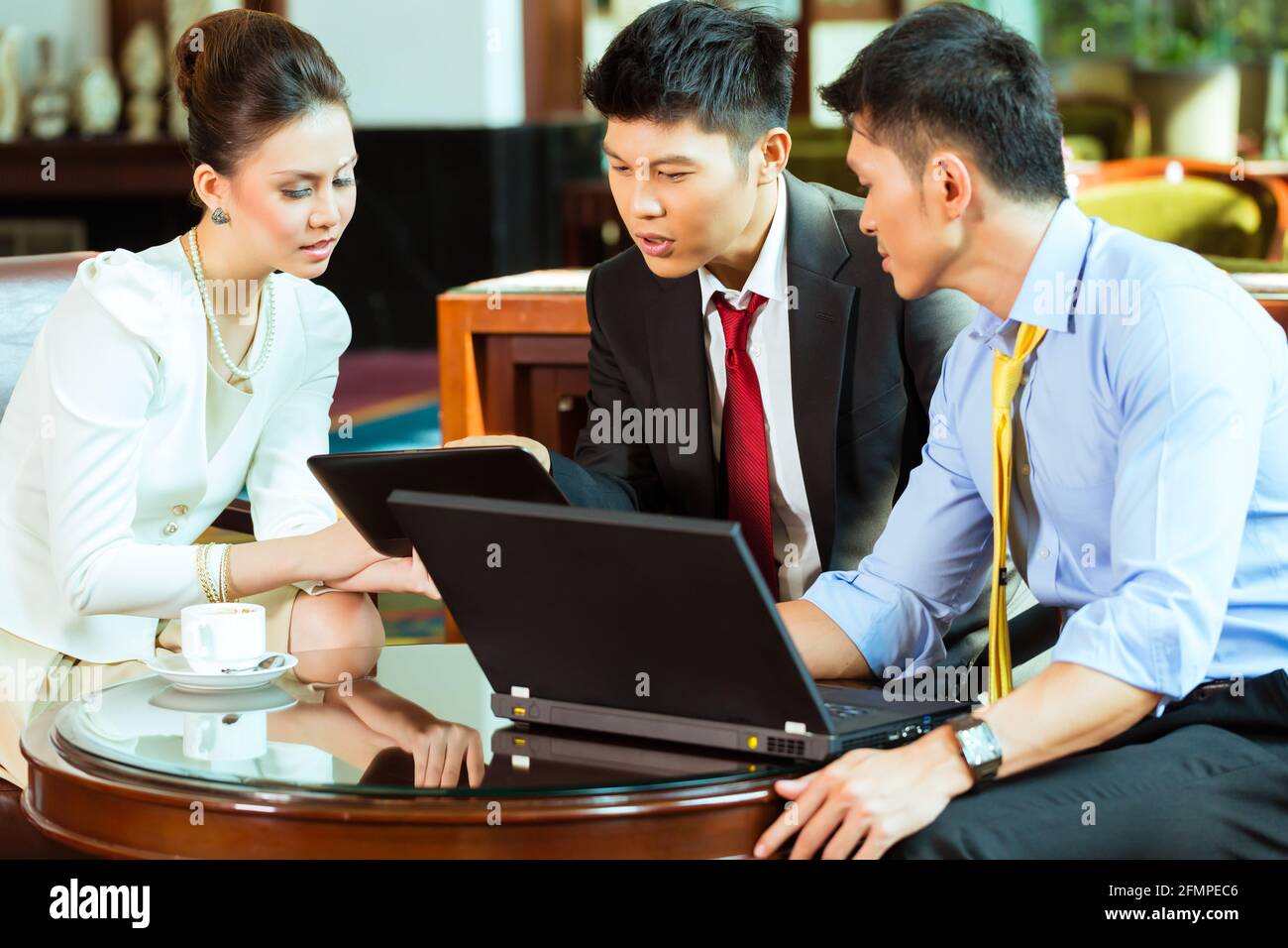Three Asian Chinese office people or businessmen and businesswoman having a business meeting in ...