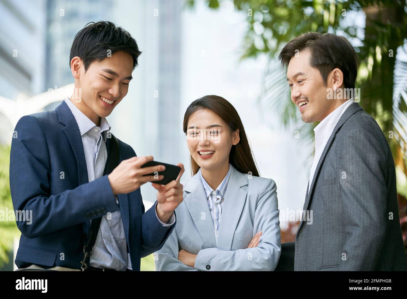 three asian business associates chatting in the street of downtown ...