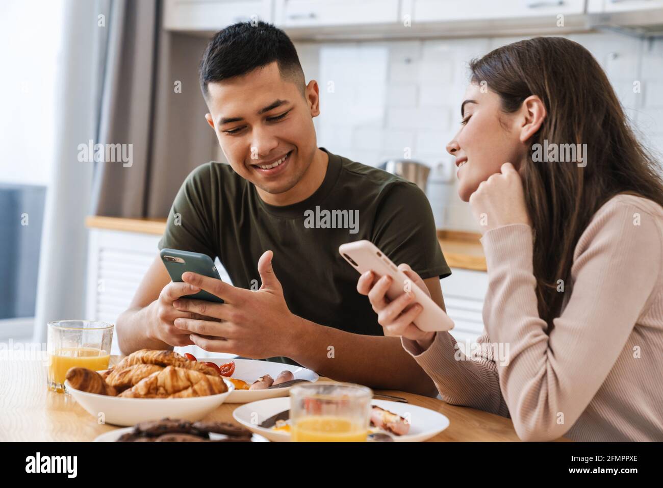 Happpy young attractive couple using mobile phones while having tasty ...