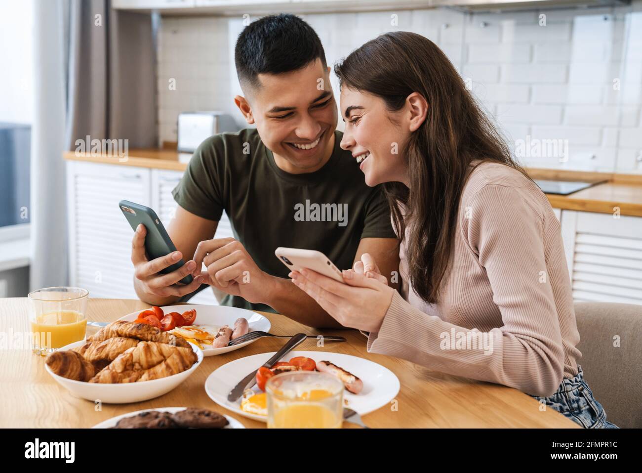 Portrait of smiling couple using smartphones and talking while having ...