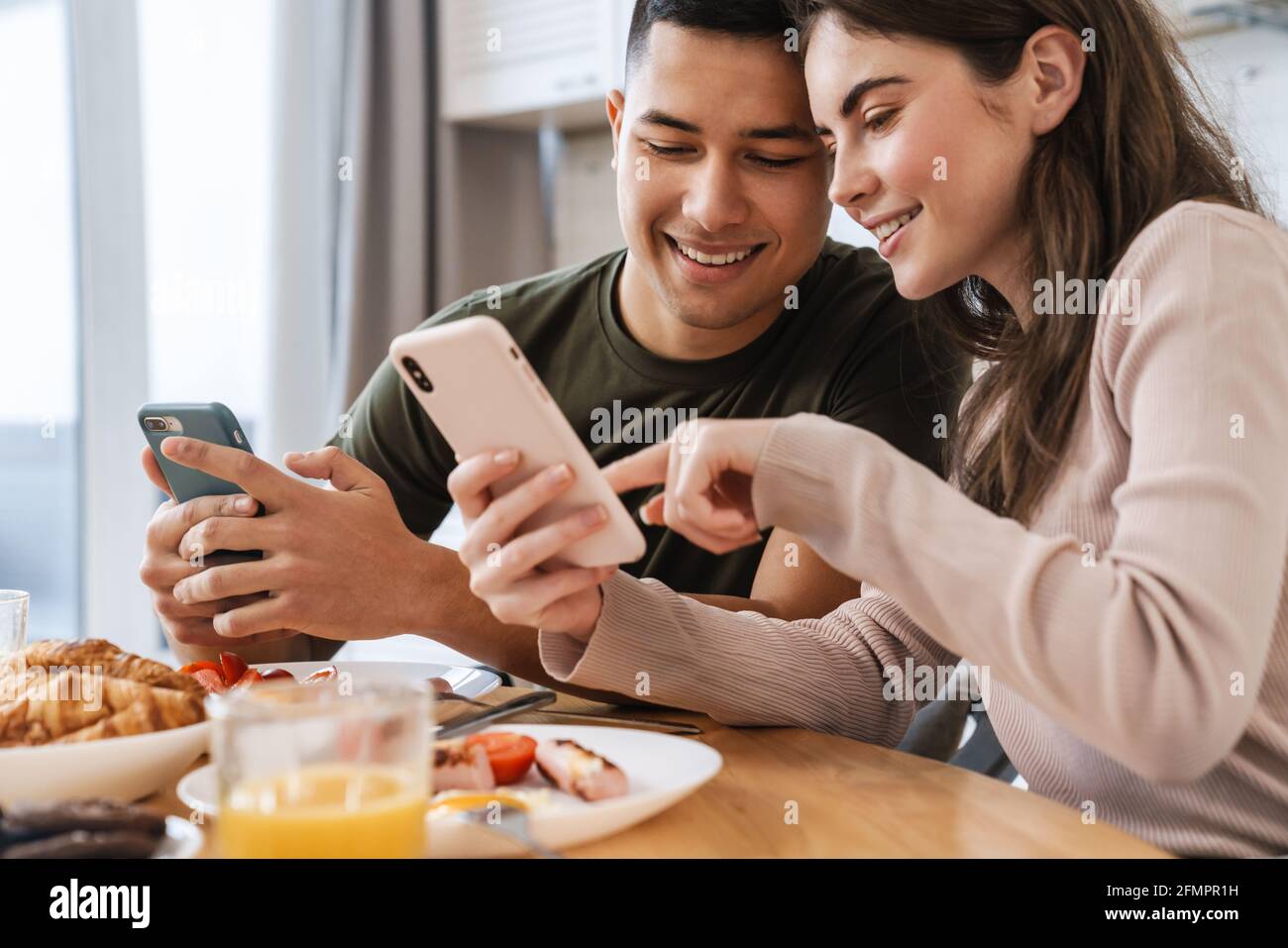 Portrait of smiling couple using smartphones and talking while having ...