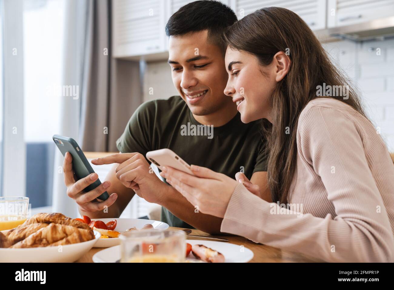 Happpy young attractive couple using mobile phones while having tasty ...