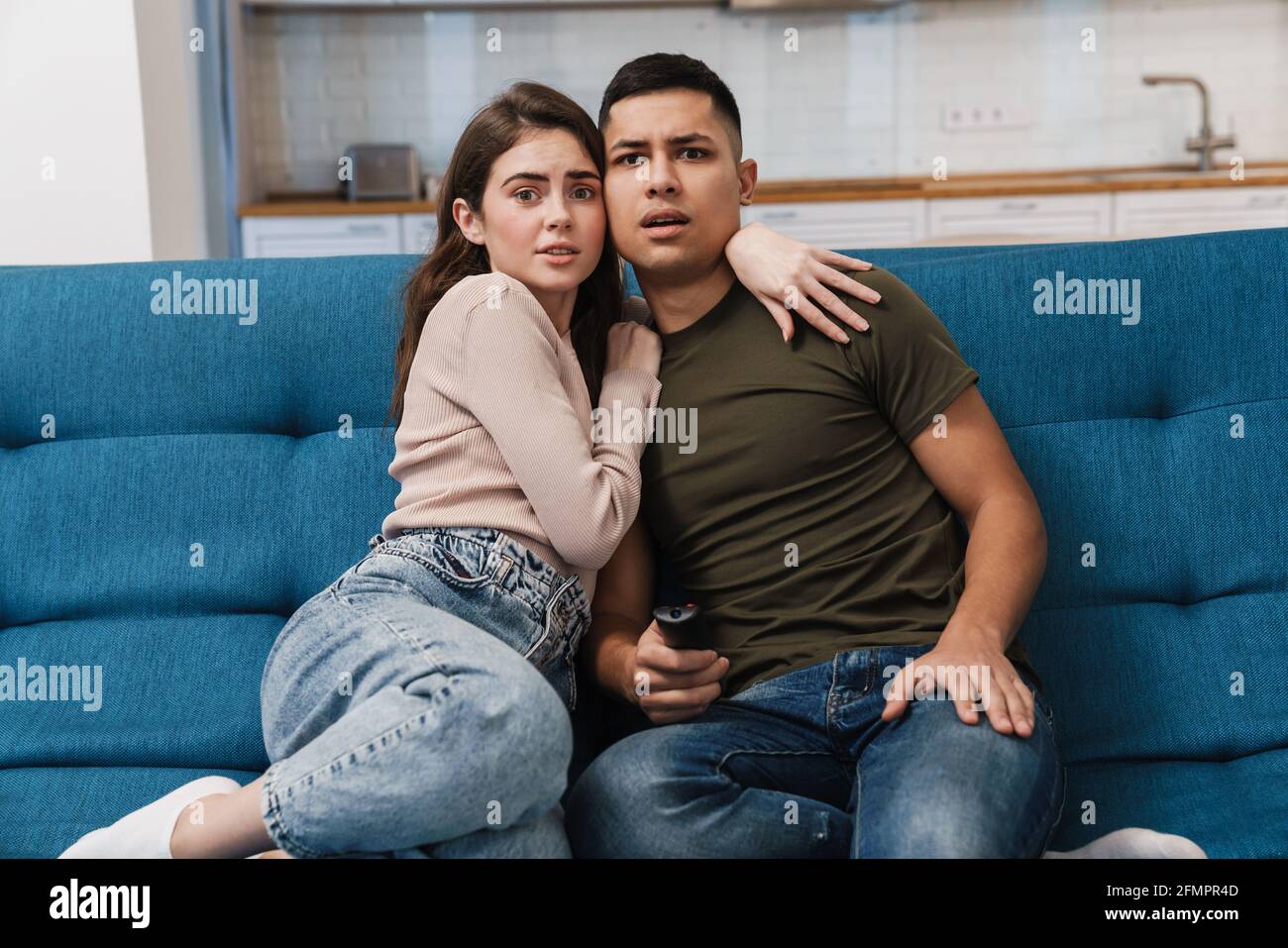 Photo of young scared couple watching tv in modern kitchen Stock Photo ...
