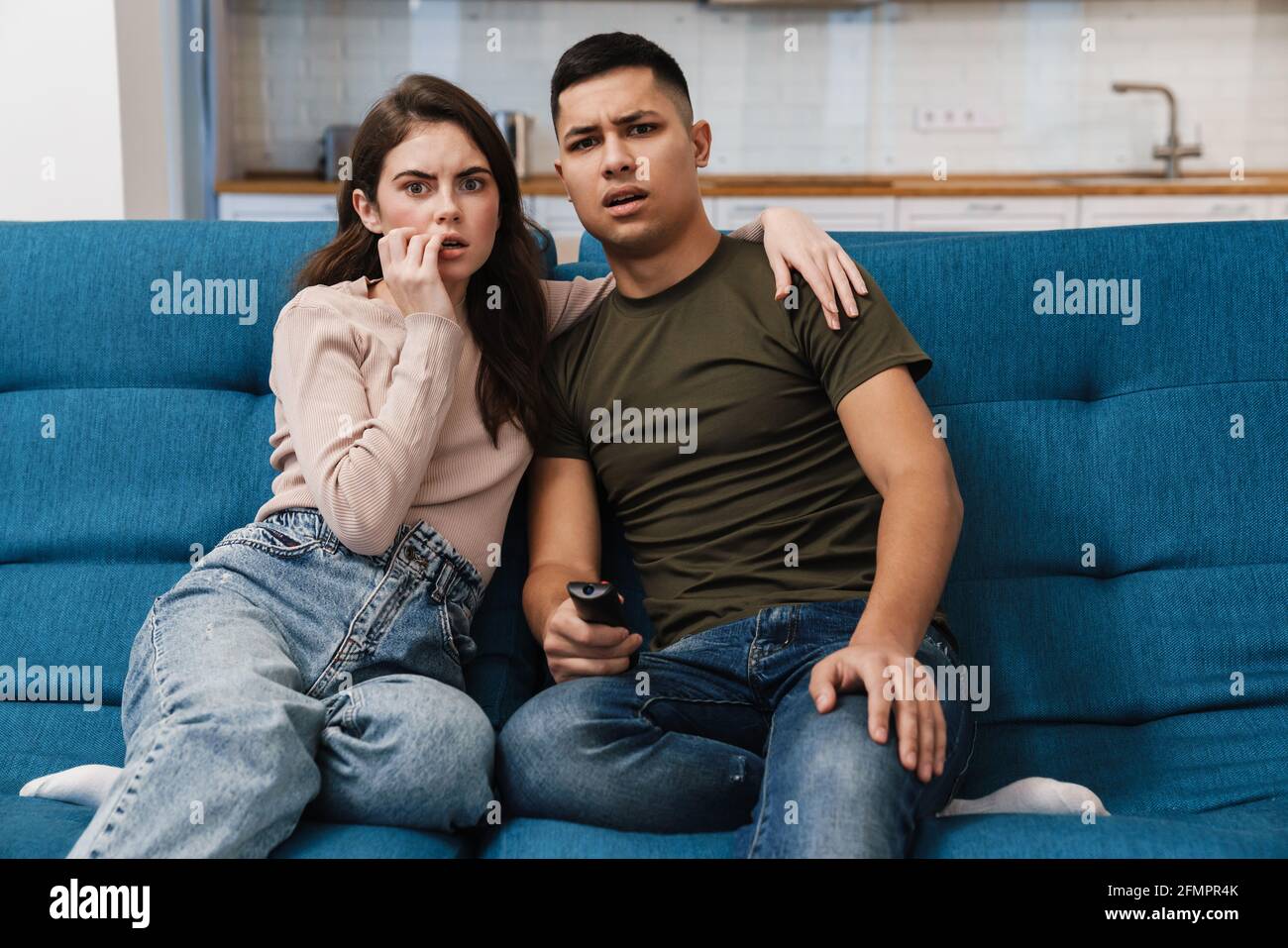 Photo of young scared couple watching tv in modern kitchen Stock Photo ...