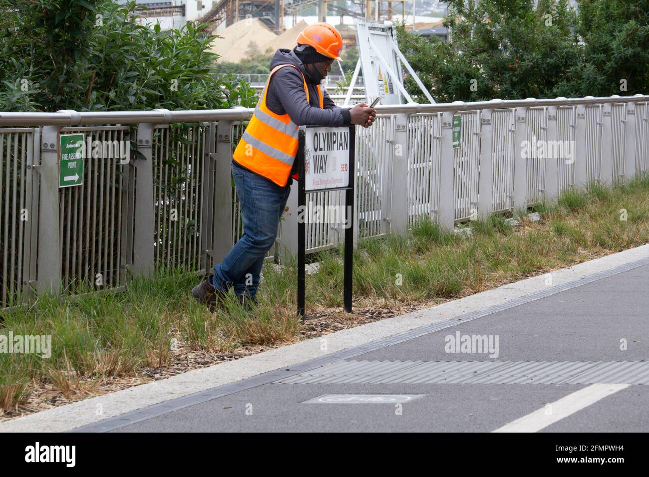 Security worker checks phone while leaning on Olympian Way street sign ...