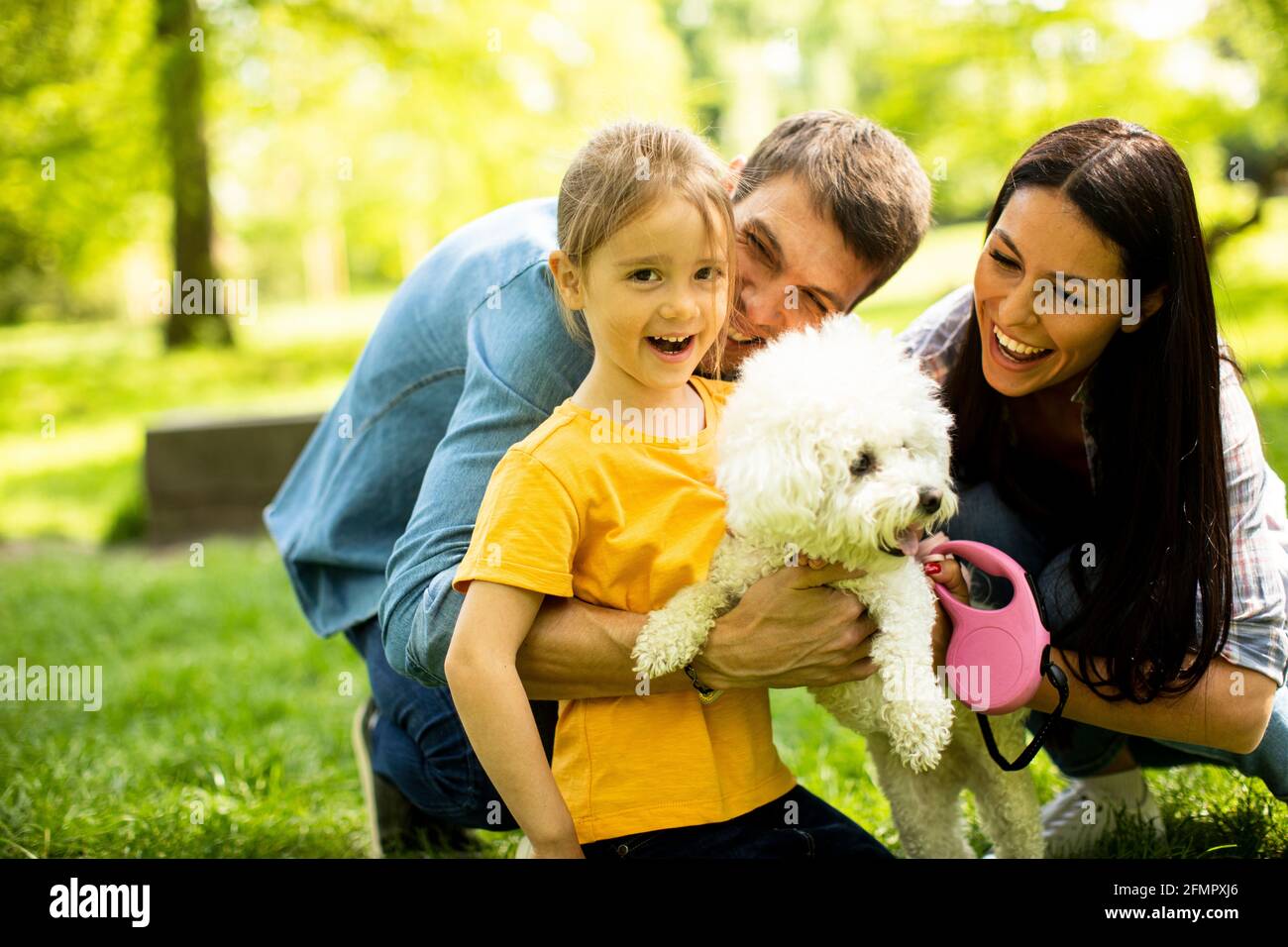 Beautiful happy family is having fun with bichon dog outdoors in the ...
