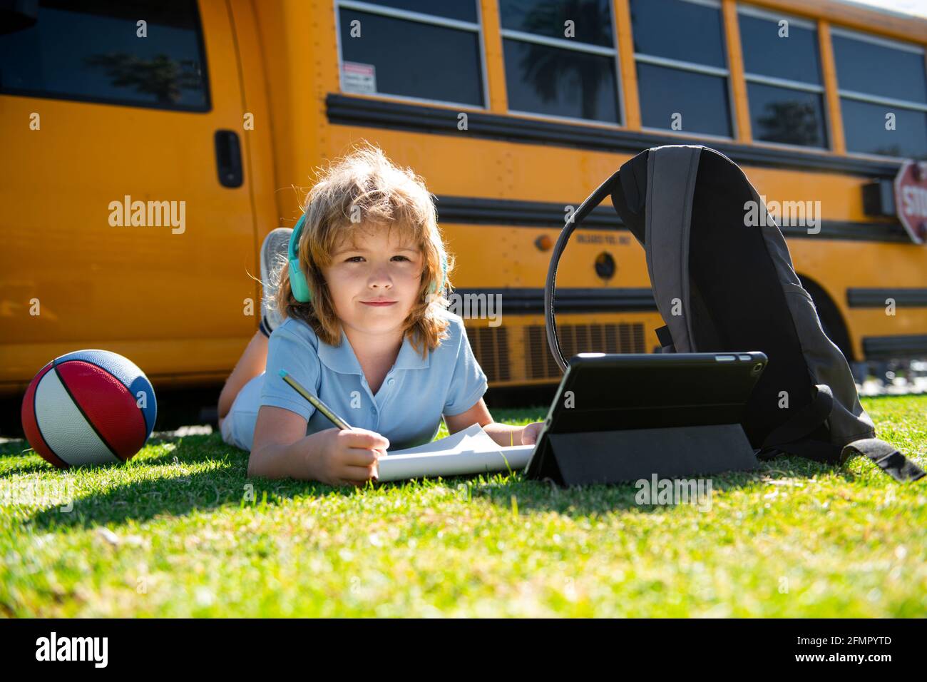 Child pupil does school homework laying on grass in the park near ...