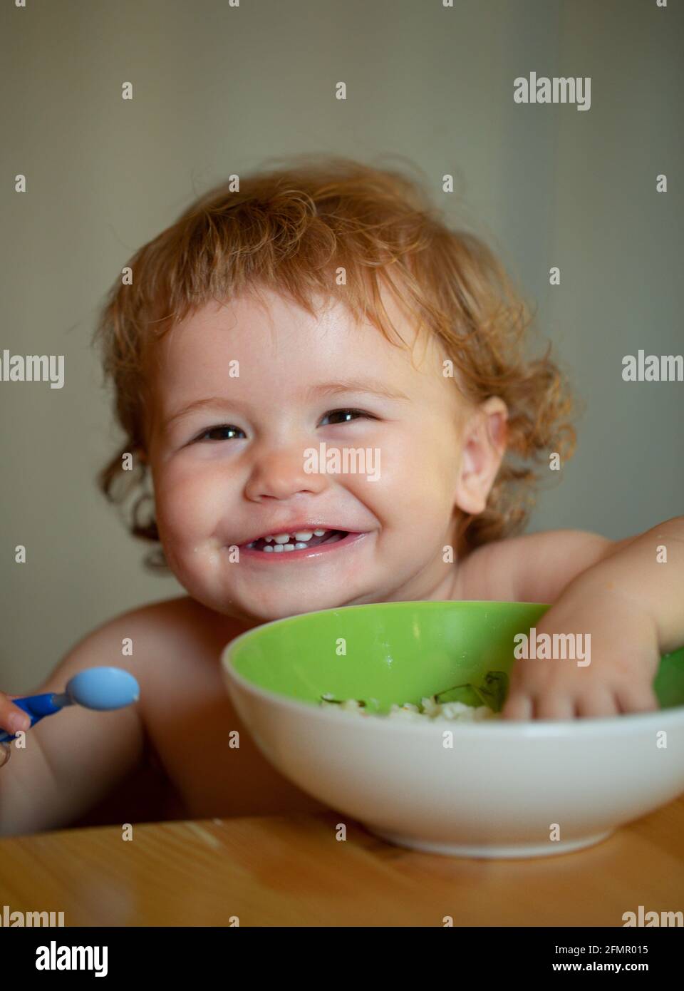 Launching child eat. Happy baby eating himself with a spoon. Smiling ...