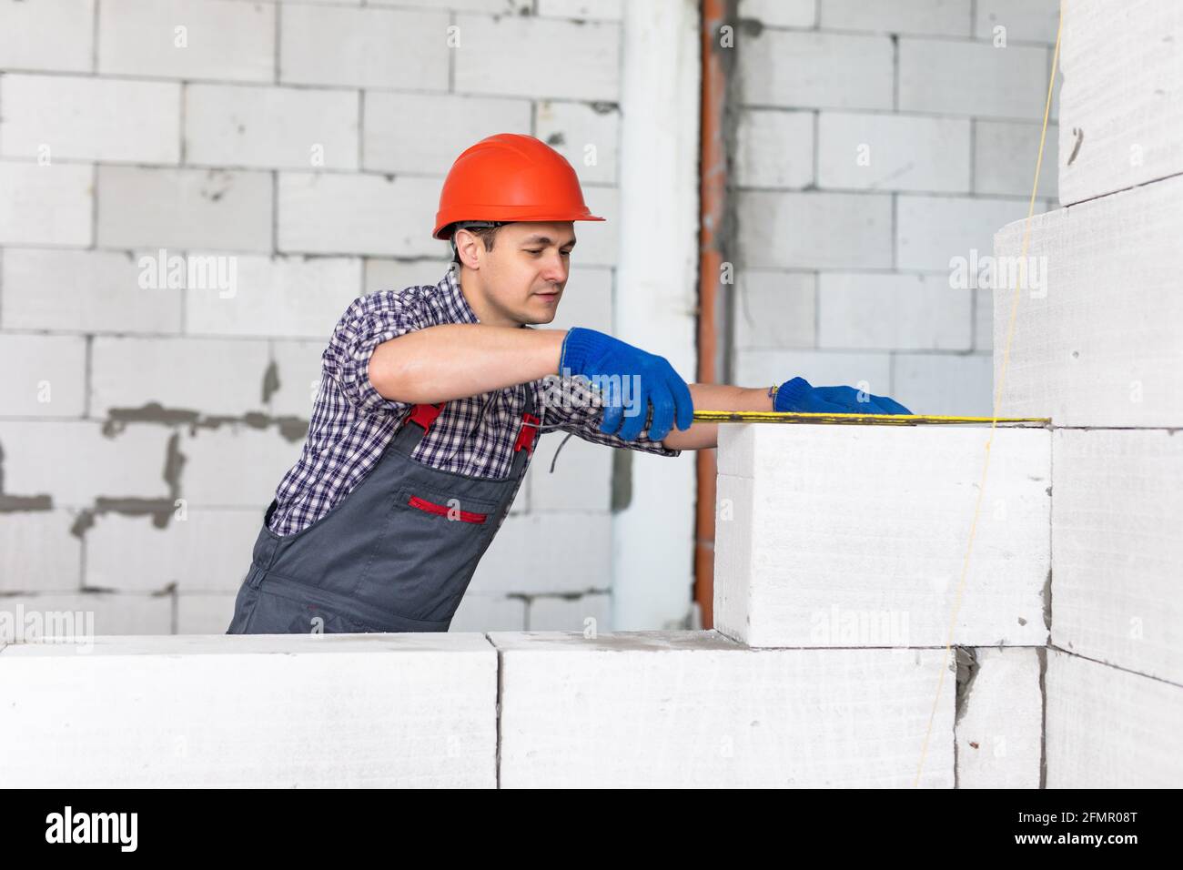 The bricklayer measures a newly built wall with a tape measure ...