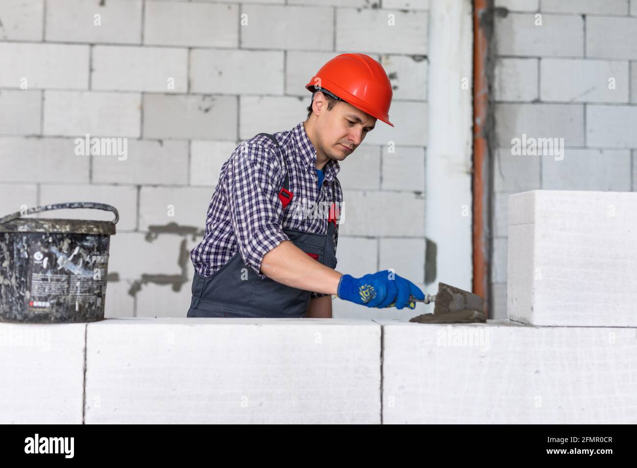 Young man builder puts on grout aerated concrete block Stock Photo - Alamy
