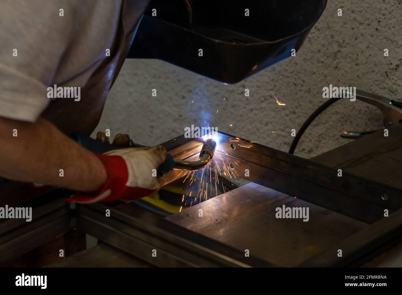 Detail of a man welding steel frames in a forgery and metal works ...