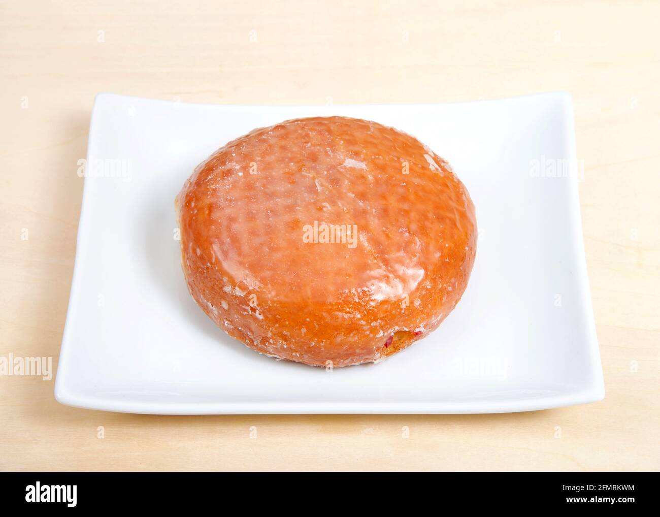 One round glazed jelly filled donut on a rectangular porcelain plate on ...