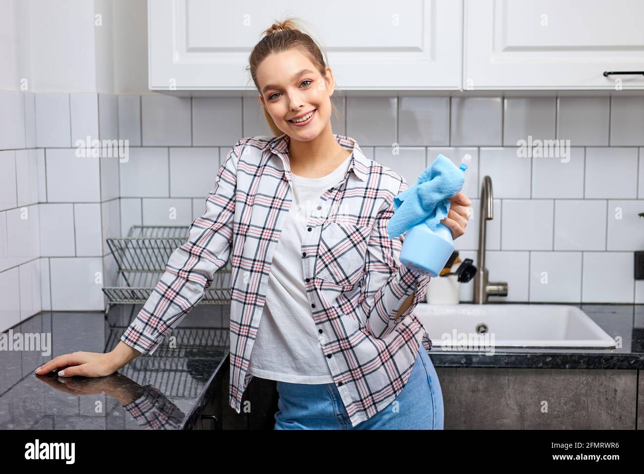 Portrait of attractive young female in checkered shirt holding rag and ...