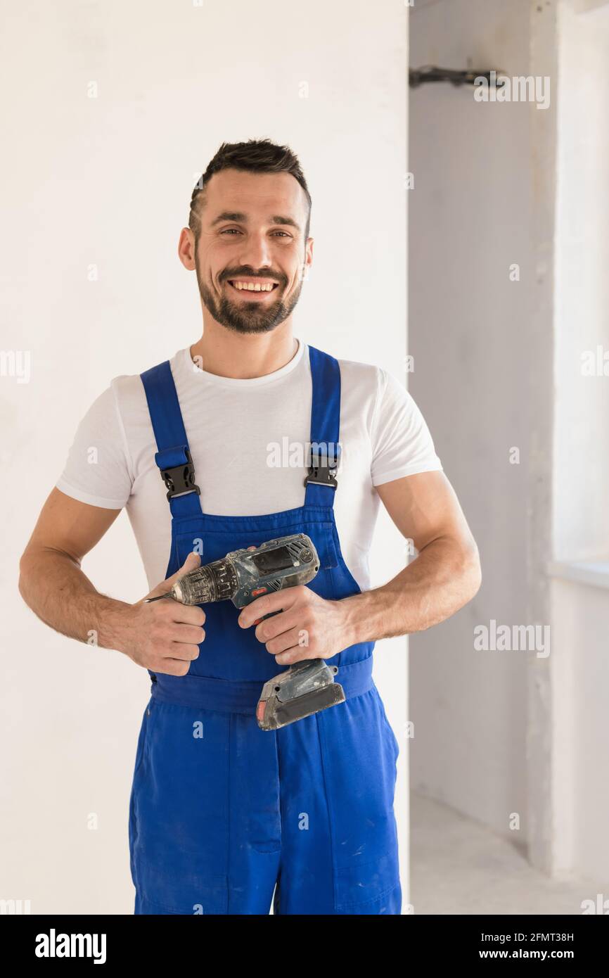 Construction worker in blue overalls posing with a drill Stock Photo ...