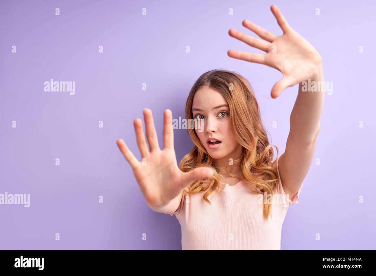 Young girl over isolated purple background scared with arms up like ...