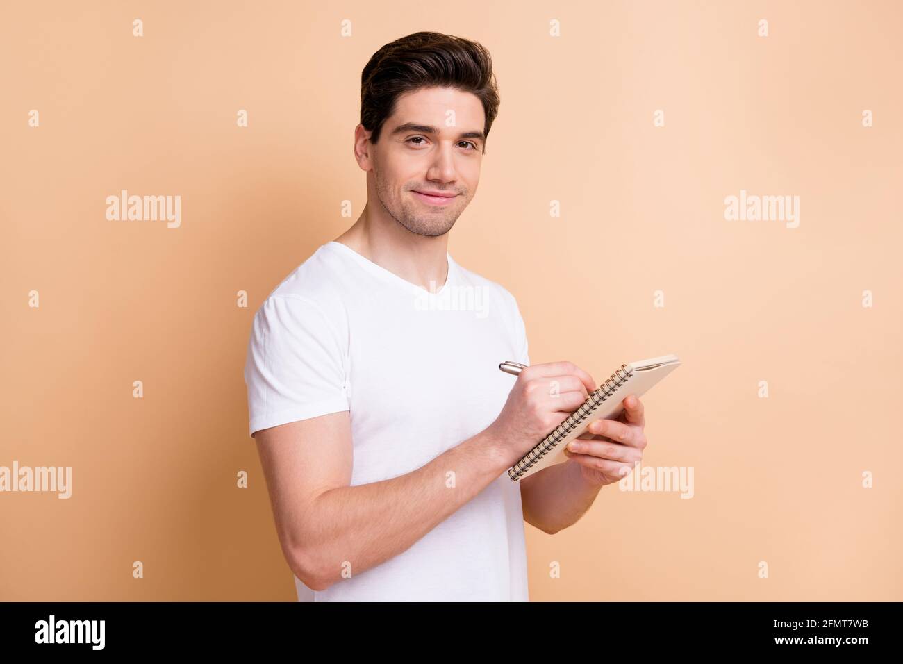 Photo of positive handsome guy writing notes in textbook look camera ...