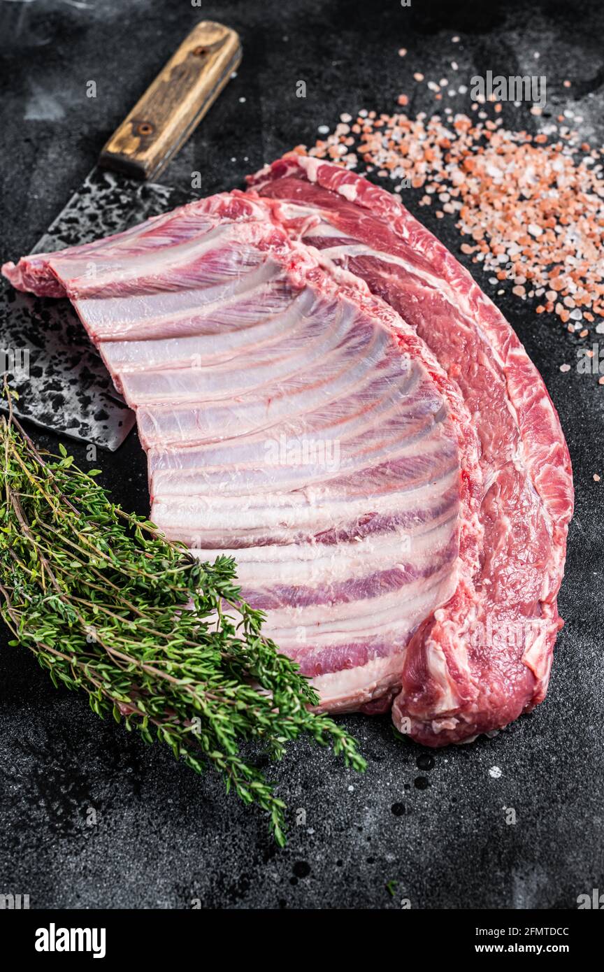 Raw rack of lamb ribs on butcher cutting board with herbs. Black ...