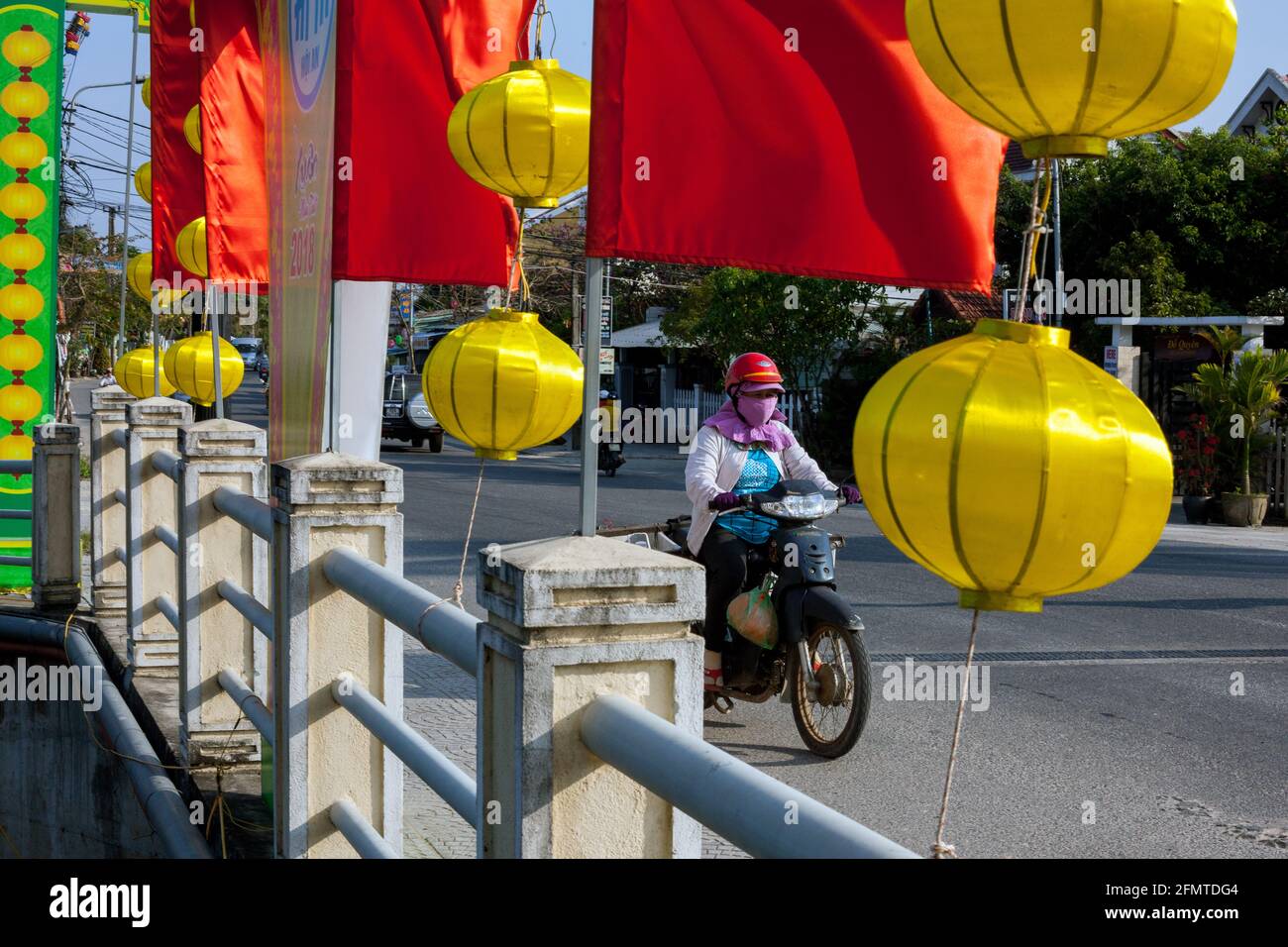 Vietnamese motorbike drives past colourful flags and lanterns displayed ...
