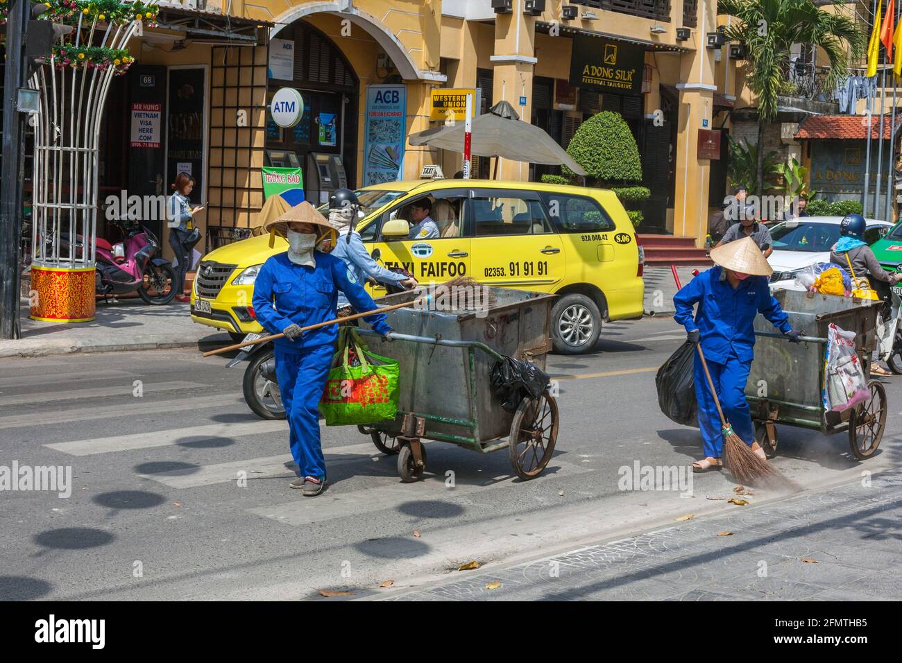 Female Vietnamese street cleaners wearing blue overalls drag their ...