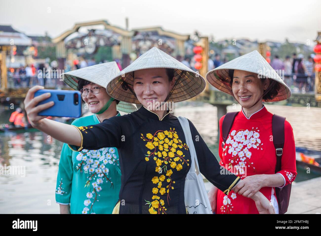 Three Vietnamese ladies wearing conical hats and ao dai traditional dresses pose for selfie by ...