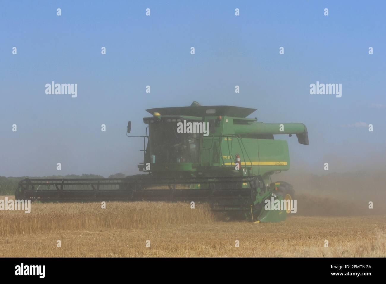 John Deere Combine cutting wheat with wheat dust in the air in a farm ...