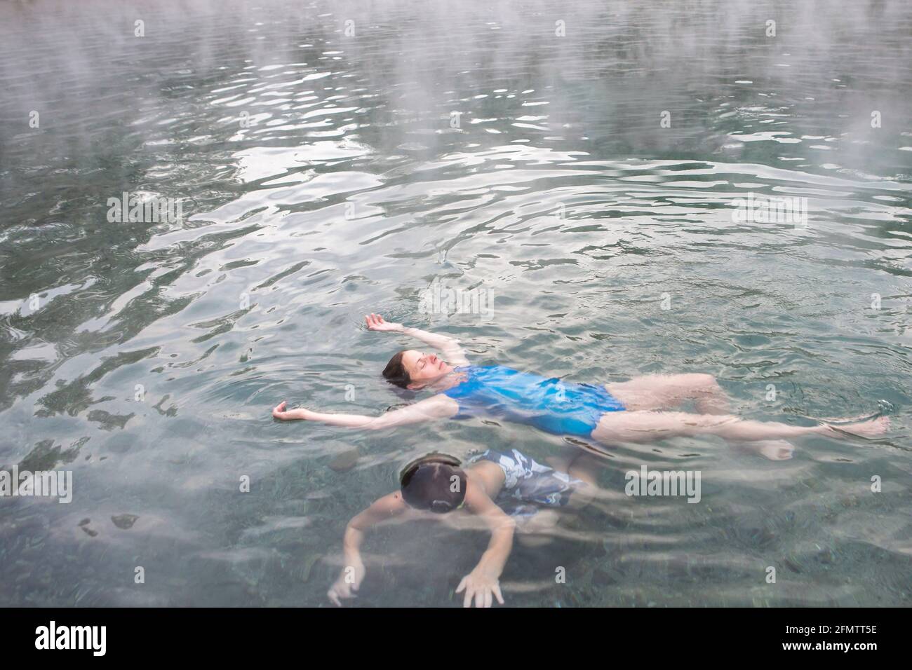 A mother and son float in Trinity Hot Springs pool with steam rising ...
