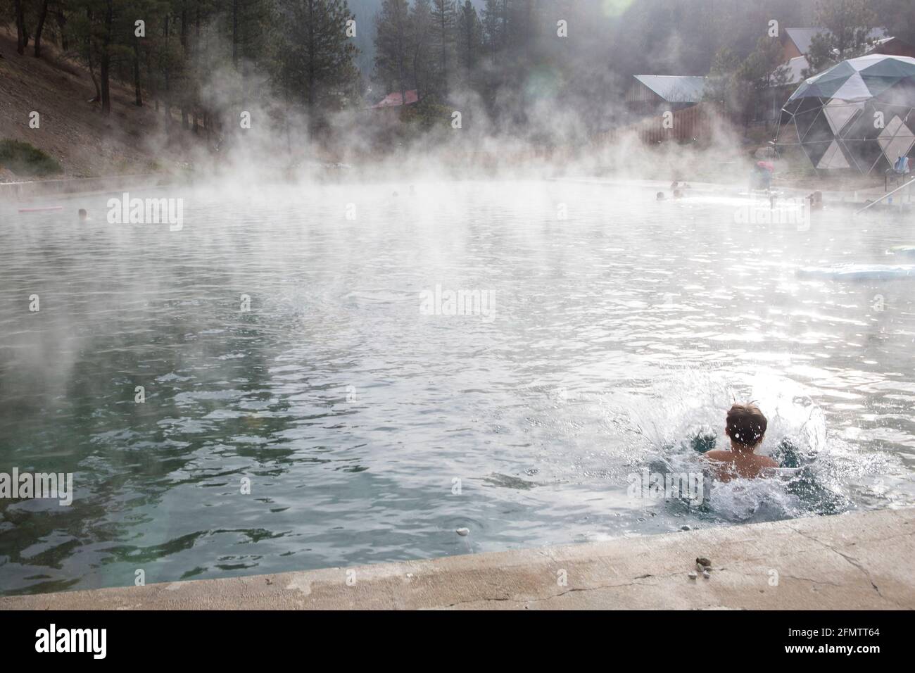 A boy jumps into a Trinity Hot Springs pool with steam rising from it ...