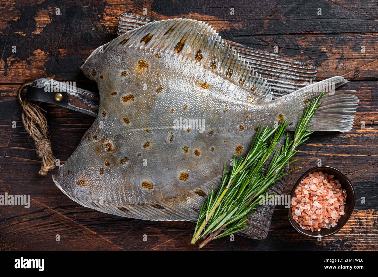 Raw plaice flatfish fish on butcher board with knife. Dark wooden ...
