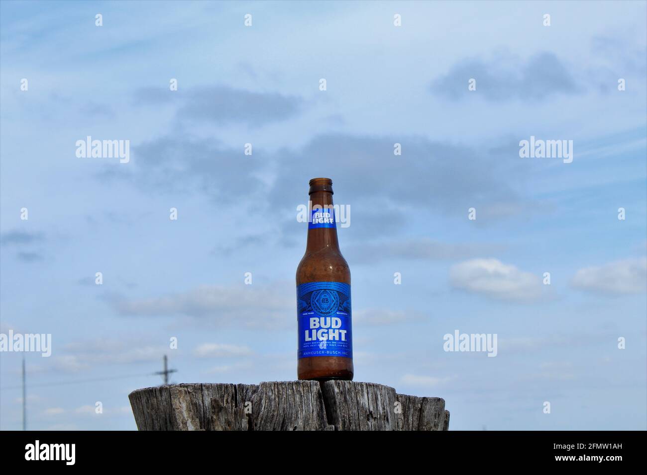 Bud Light beer bottle shot closeup on a post with blue sky and clouds ...