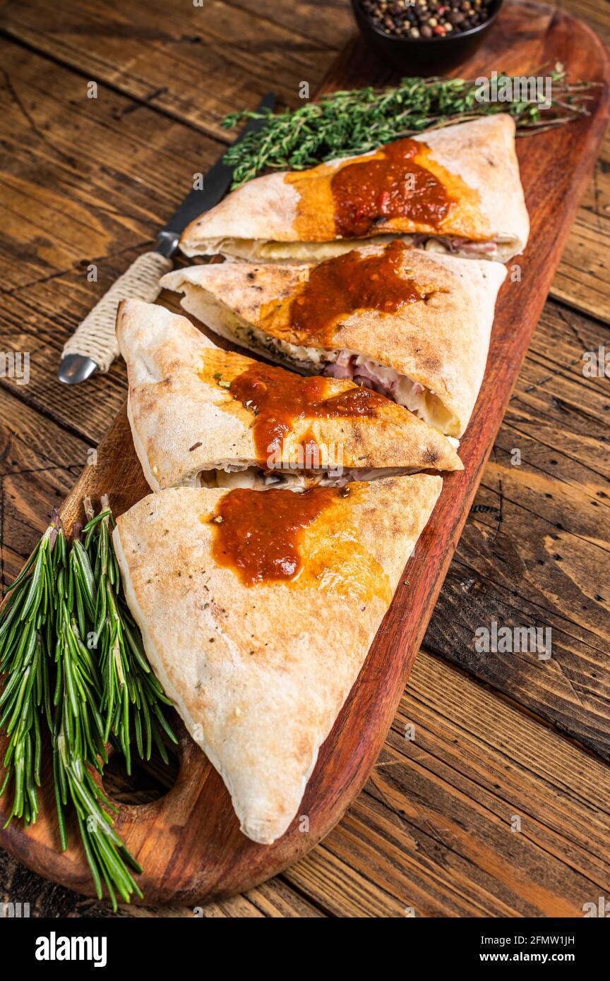 Cut and sliced Calzone closed pizza with ham and cheese on wooden board ...