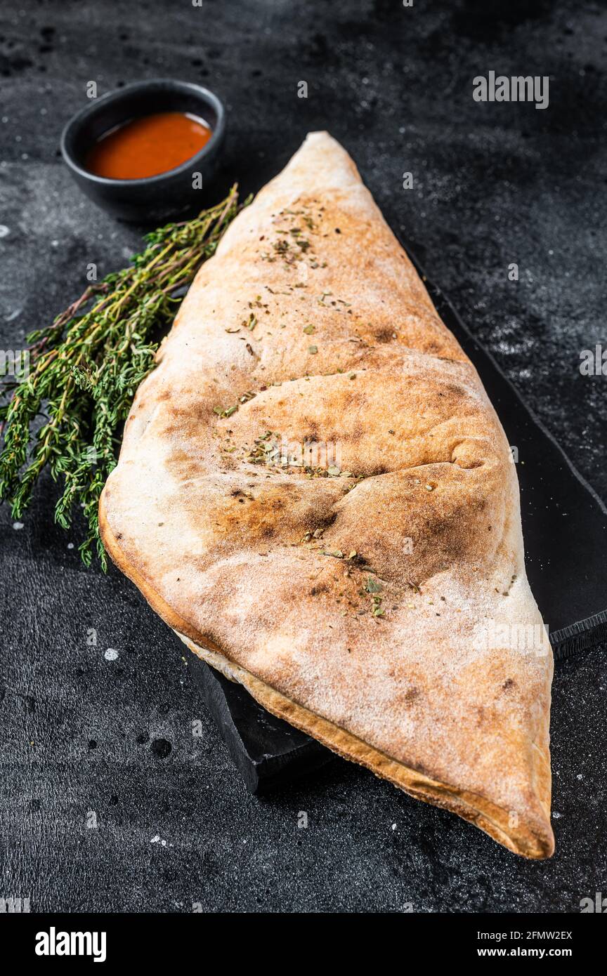 Calzone closed pizza with ham and cheese. Black background. Top view ...