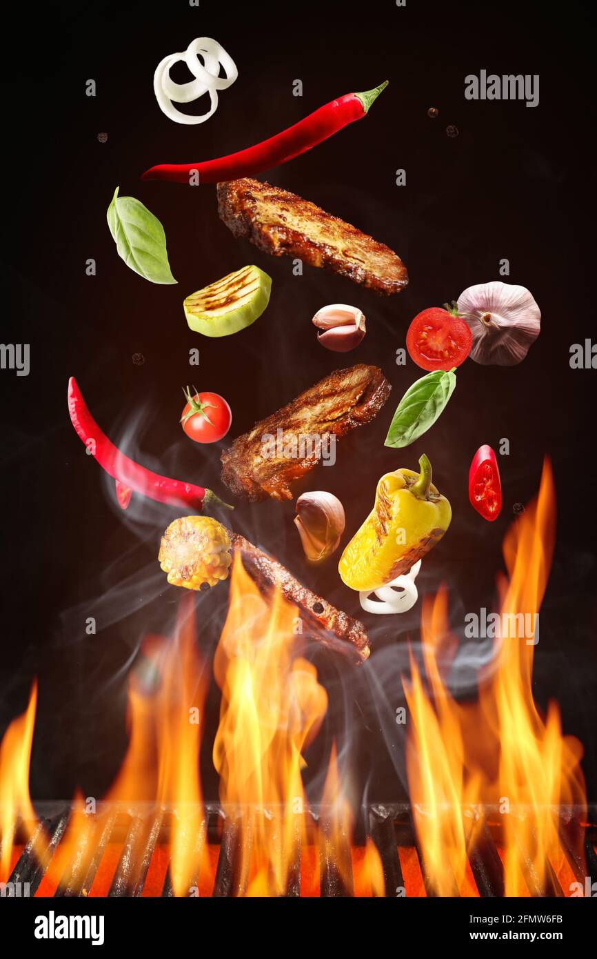 Flying beef stakes and vegetables above barbecue grill with fire on ...