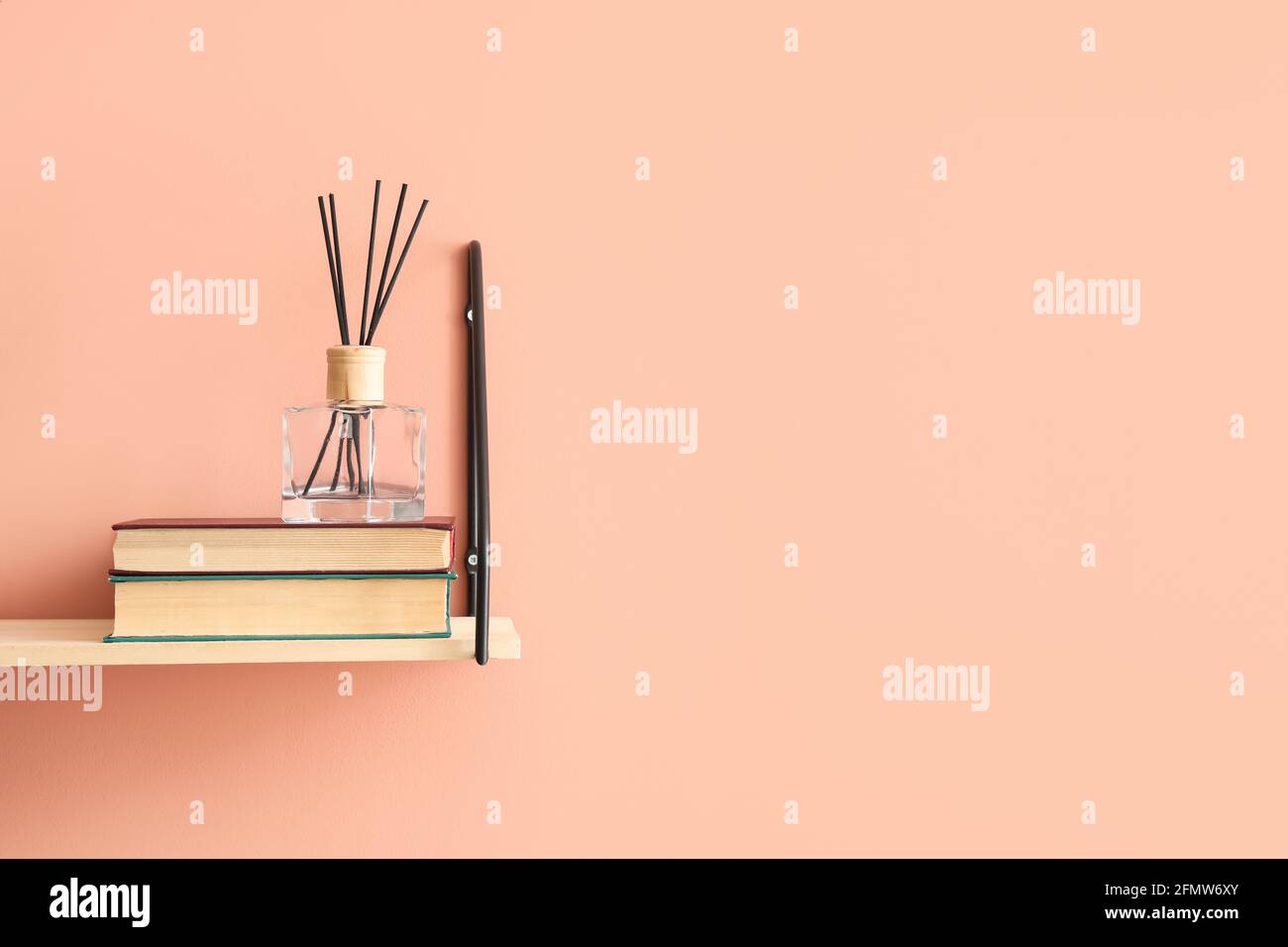 Shelf with books and reed diffuser hanging on color wall Stock Photo ...