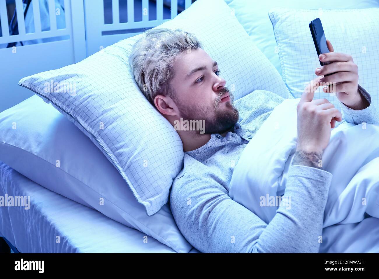 Young man with mobile phone in bed at night. Concept of addiction to ...