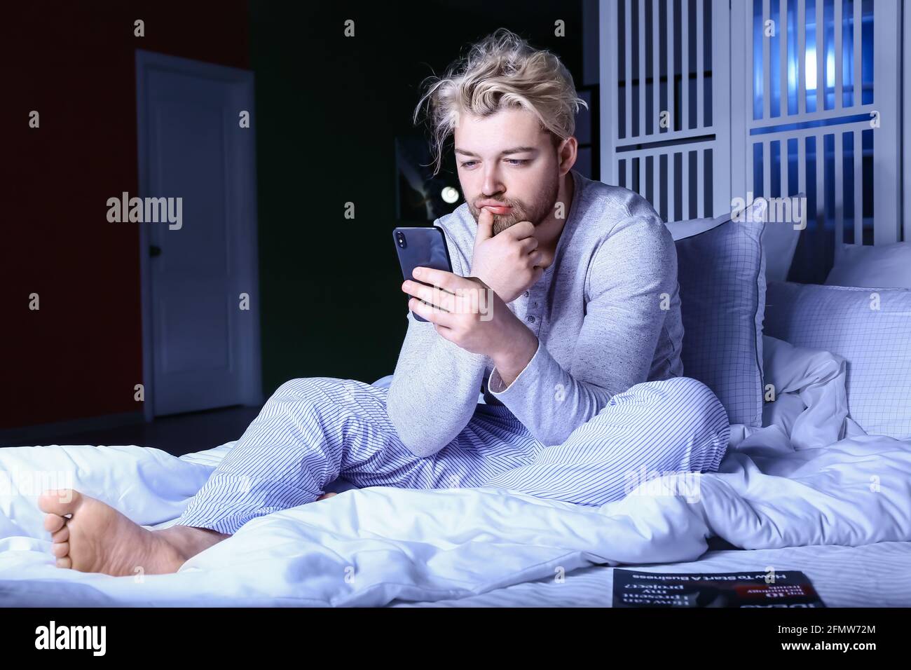 Young man with mobile phone in bed at night. Concept of addiction to ...