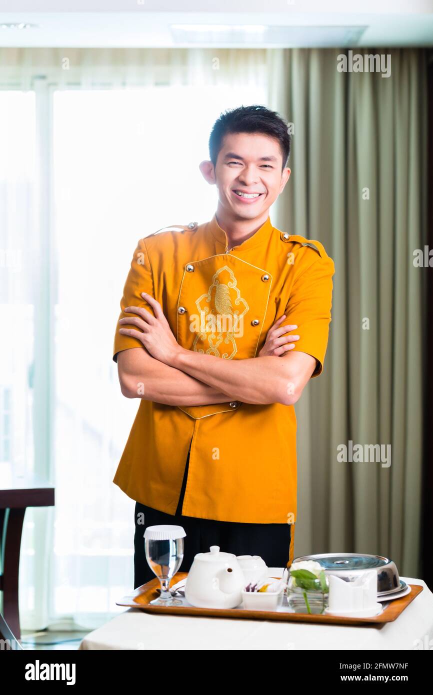 Asian Chinese room service waiter or steward serving guests food in a ...