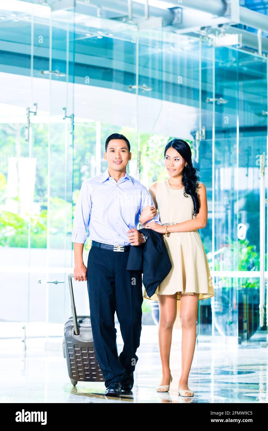 Asian couple walking in hotel lobby with suitcase Stock Photo - Alamy