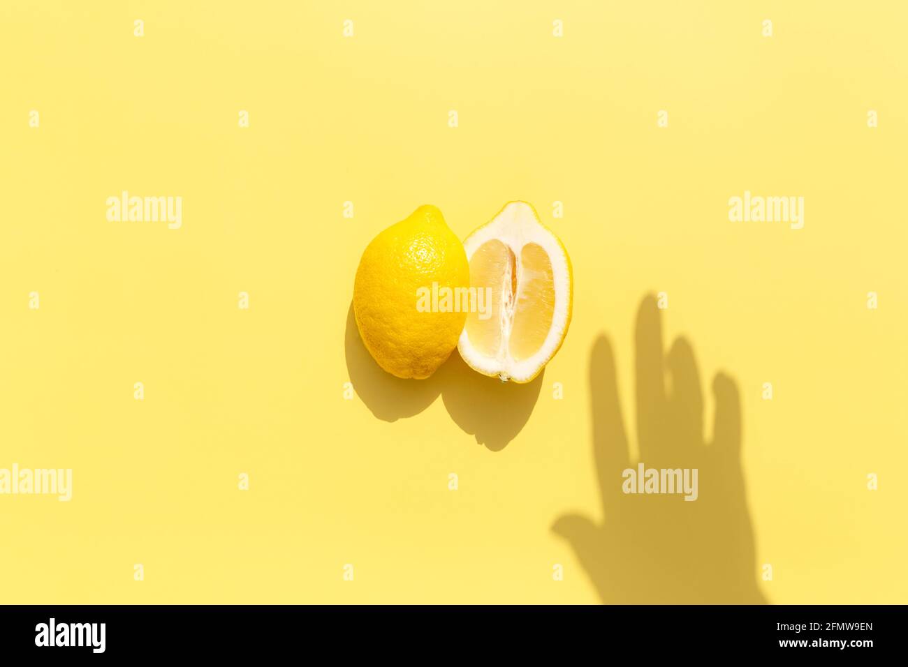 Two halved cuts of lemon with shadow from hand on yellow background ...