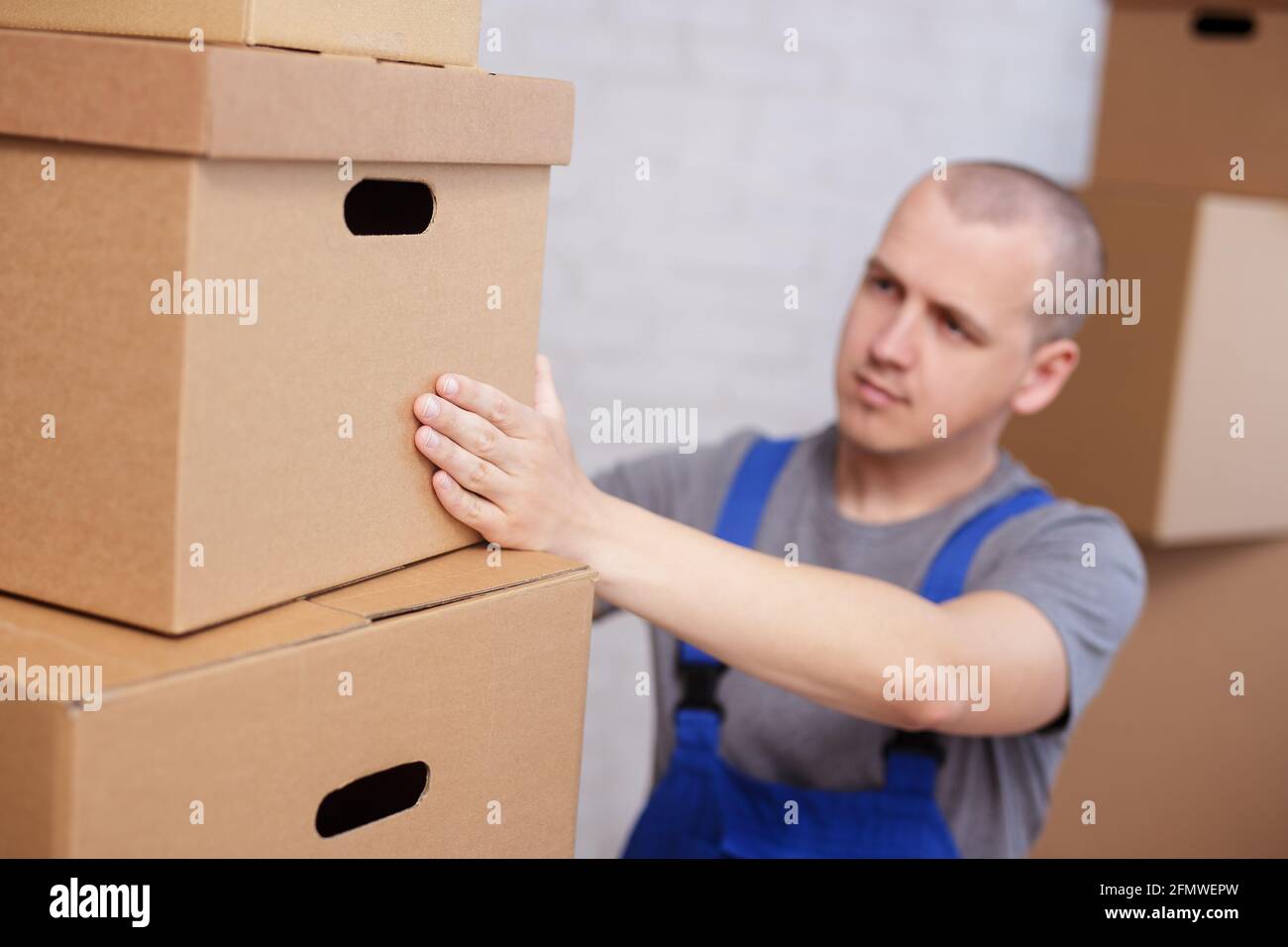 young man worker in uniform taking big box from shelf in warehouse ...