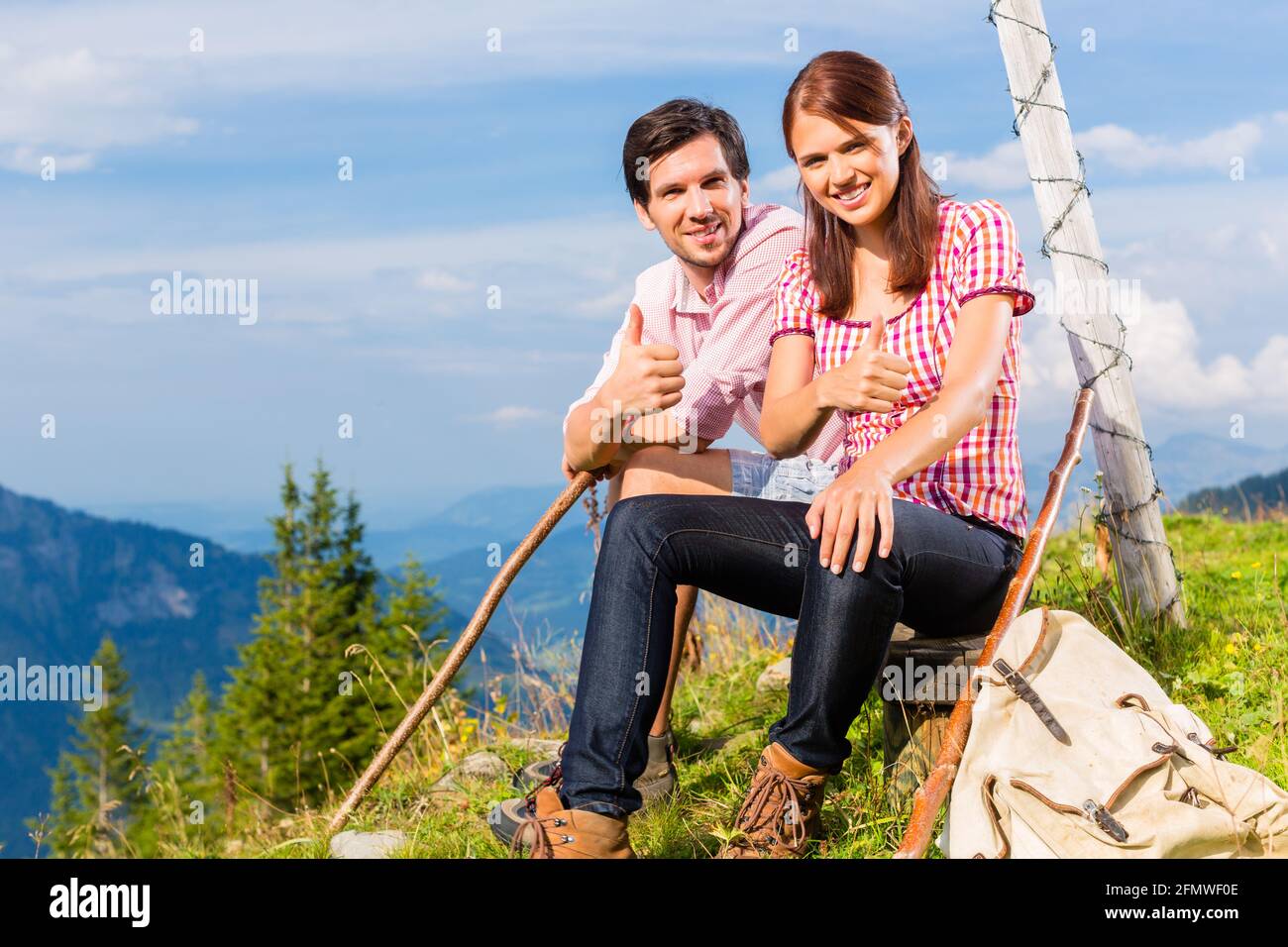 Hiking - Young couple sitting on mountain summit at cross in the ...