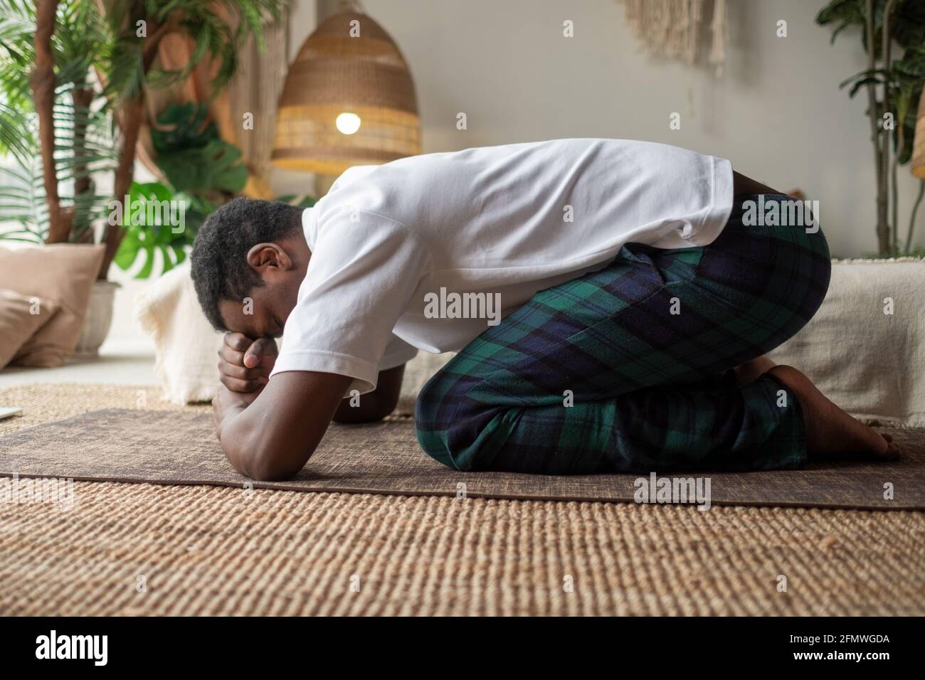 African man doing yoga at home, having rest in balasana or child pose ...