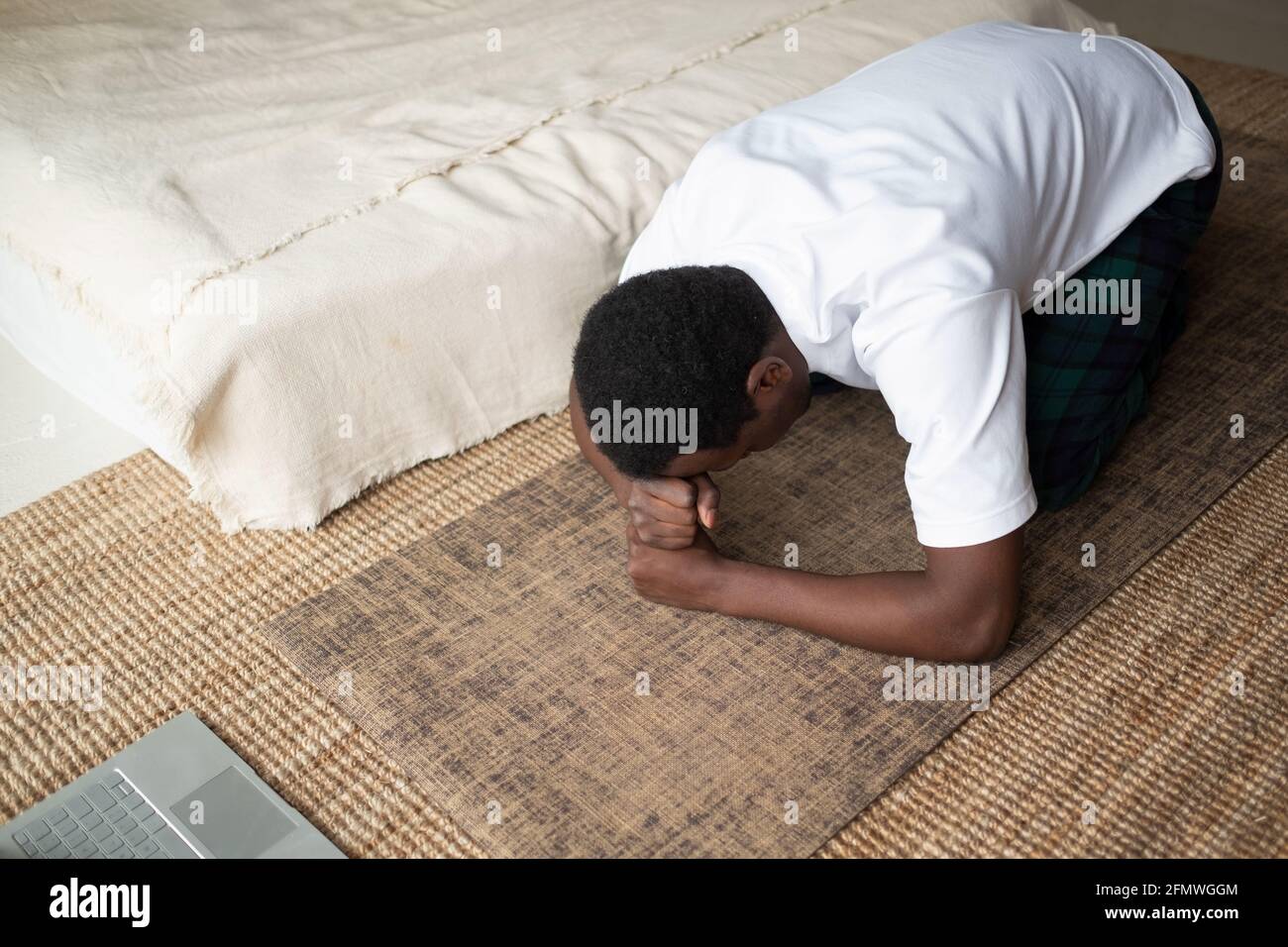 African man doing yoga at home, having rest in balasana or child pose ...
