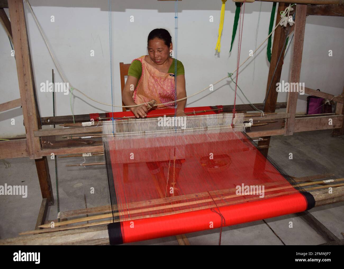 A woman weaver uses a loom to make a hand woven red saree at her ...